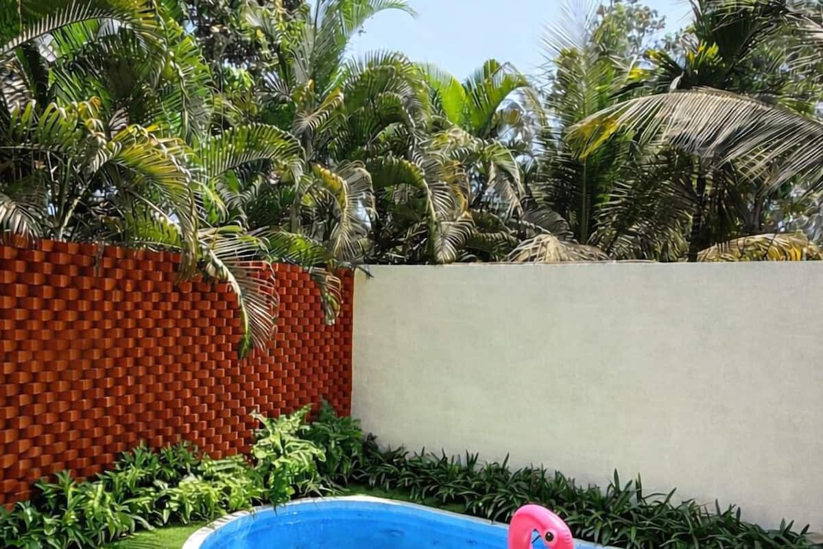 Piscina com um flutuador em formato de flamingo rosa, rodeada por grama verde e palmeiras.