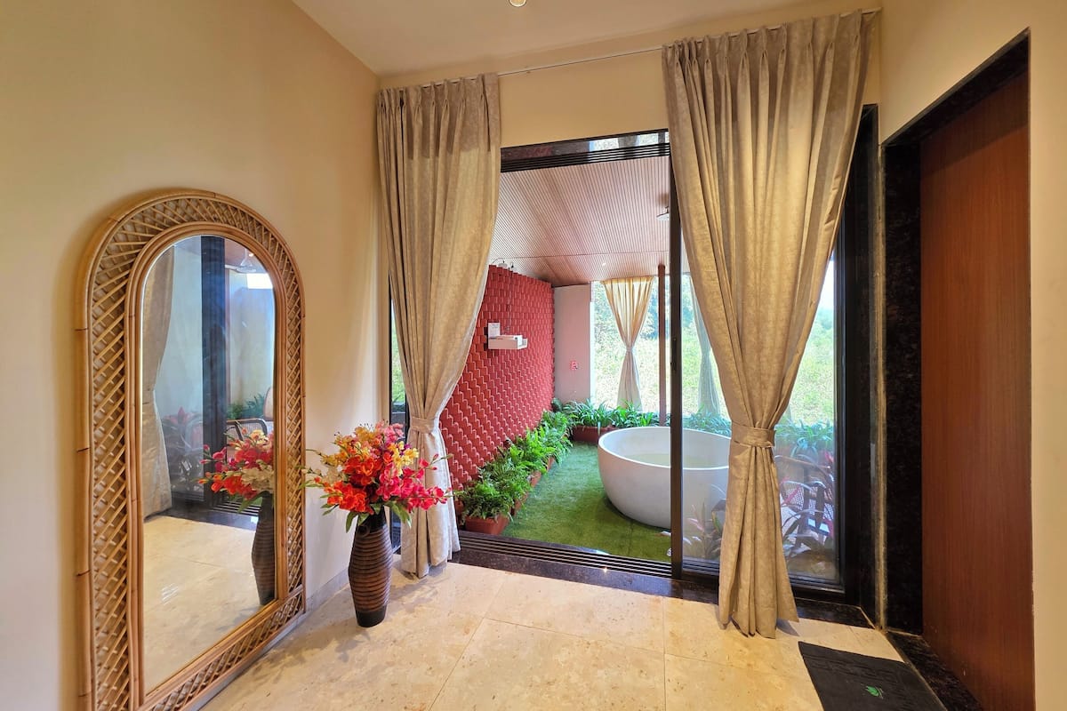 Um corredor com um espelho grande, um vaso com flores e vista para um jardim com hidromassagem.