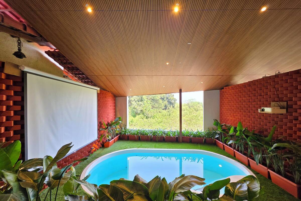 Uma área de piscina com teto de madeira, paredes de tijolos vermelhos e plantas verdes.