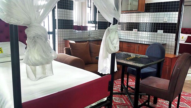 Um quarto com uma cama, uma mesa, uma cadeira, um sofá e um tapete estampado.