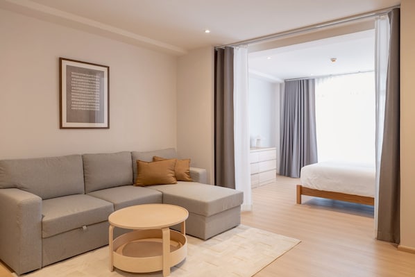 Uma sala de estar moderna com um sofá cinzento, uma mesa de centro redonda e uma cama com estrutura de madeira.