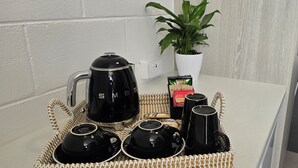 Uma bancada de cozinha com cafeteira, saquinhos de chá e canecas pretas.