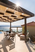 Um terraço com mesa, cadeiras, um vaso de planta e vista para o mar.