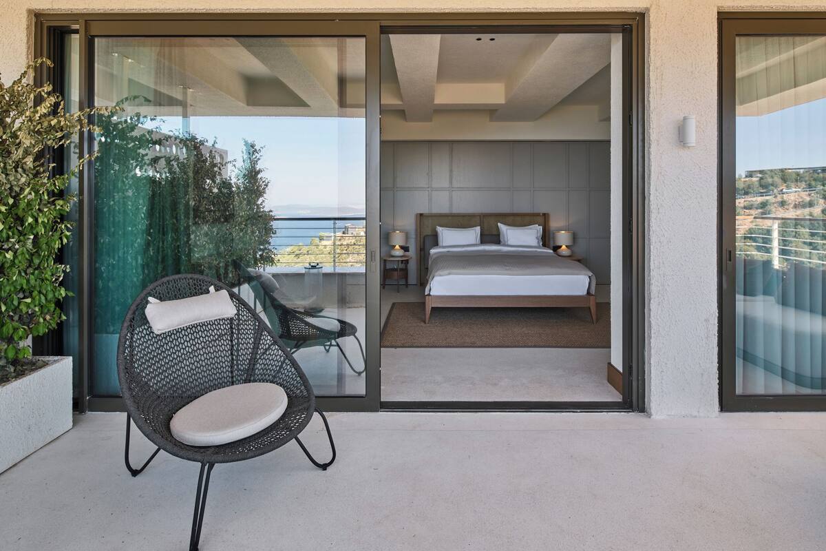 Uma varanda com cama, cadeira e vista para o mar.