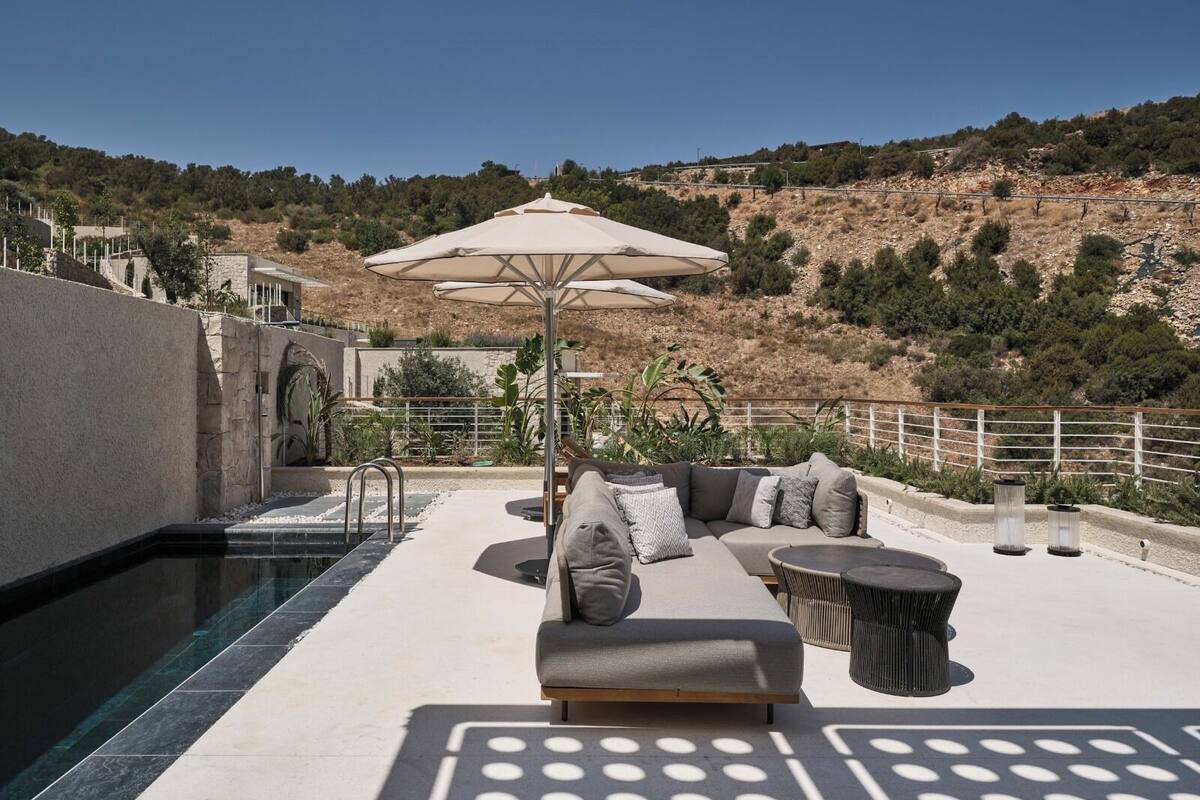 Área de piscina no terraço com espaço de estar, incluindo um sofá e cadeiras, e um grande guarda-sol para dar sombra.