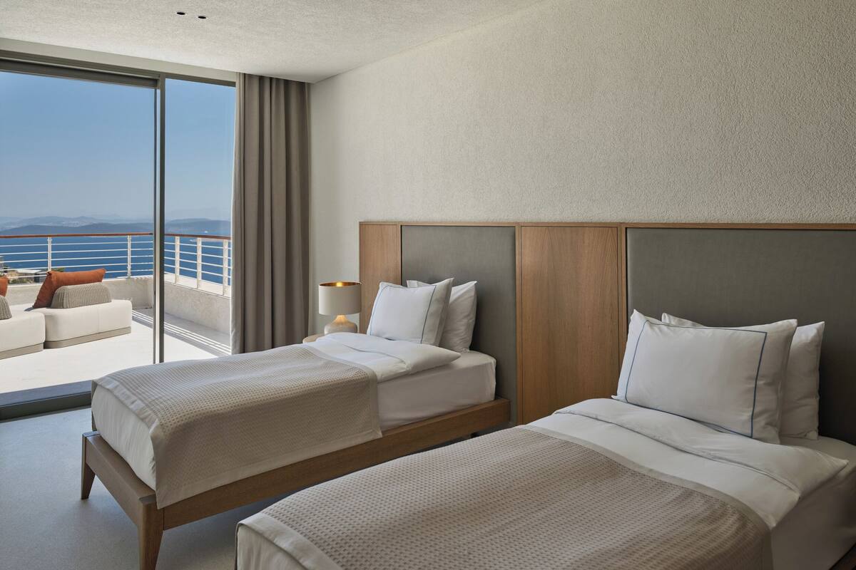 Quarto de hotel com duas camas, uma varanda com vista para o mar e uma janela grande.