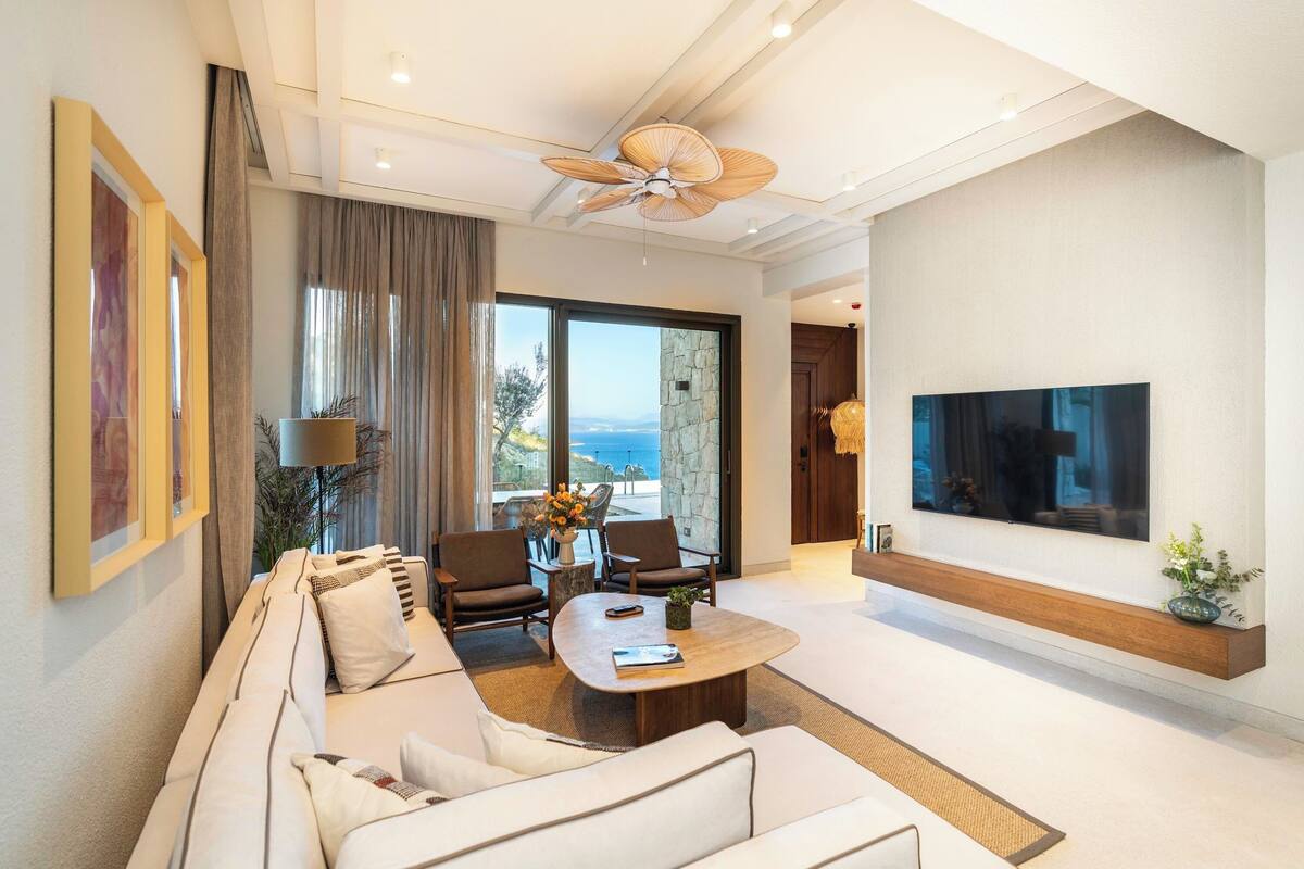 Uma sala de estar moderna com sofá, cadeiras, mesa de centro, televisão e uma janela grande com vista.