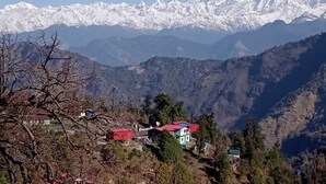 Paisagem montanhosa com picos nevados ao fundo e um conjunto de casas com telhados vermelhos em primeiro plano.