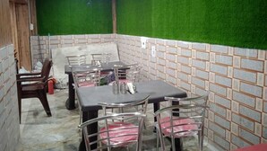 Uma área de refeições com paredes de tijolo, grama sintética verde e mesas e cadeiras de metal.