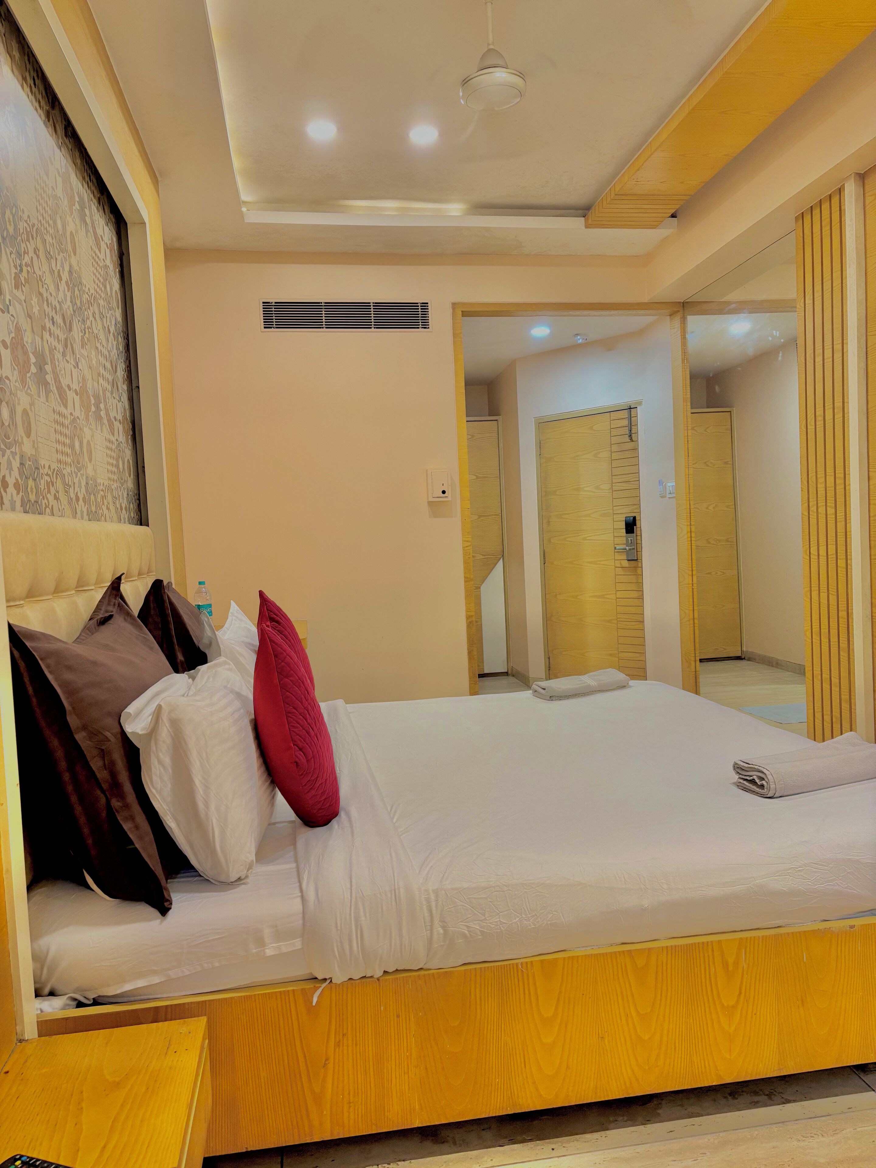 Cama bem arrumada com almofadas, mesa de cabeceira com controle remoto e cabeceira de madeira.