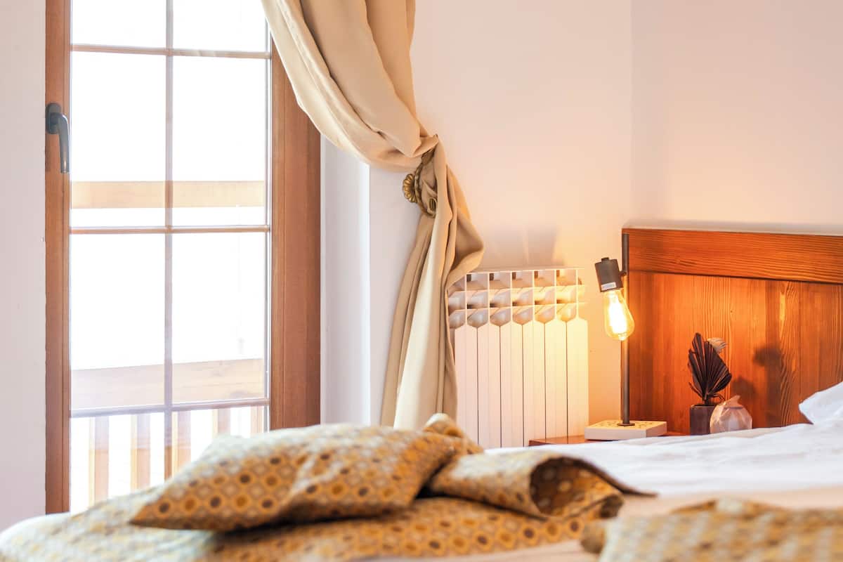 Quarto de hotel com cama, cortinas, luminária de cabeceira e janela.