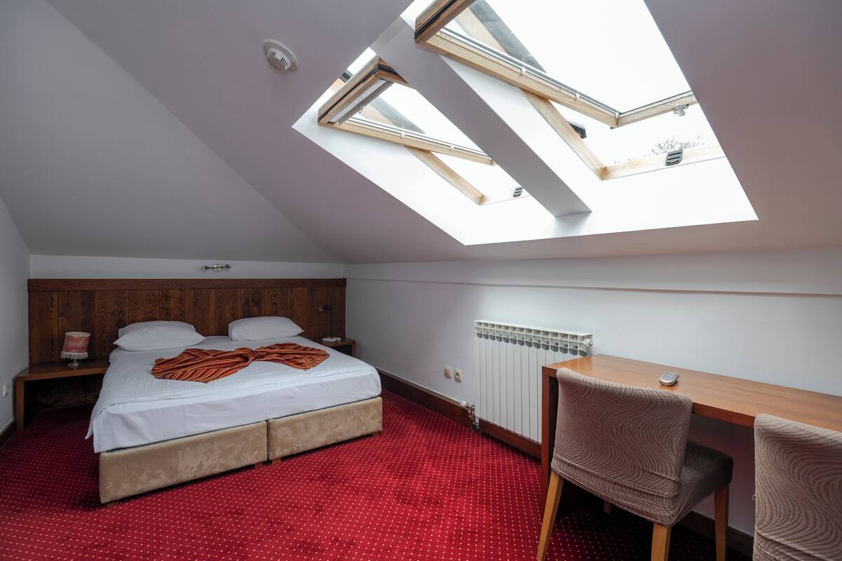 Quarto com cama, escrivaninha e claraboia.