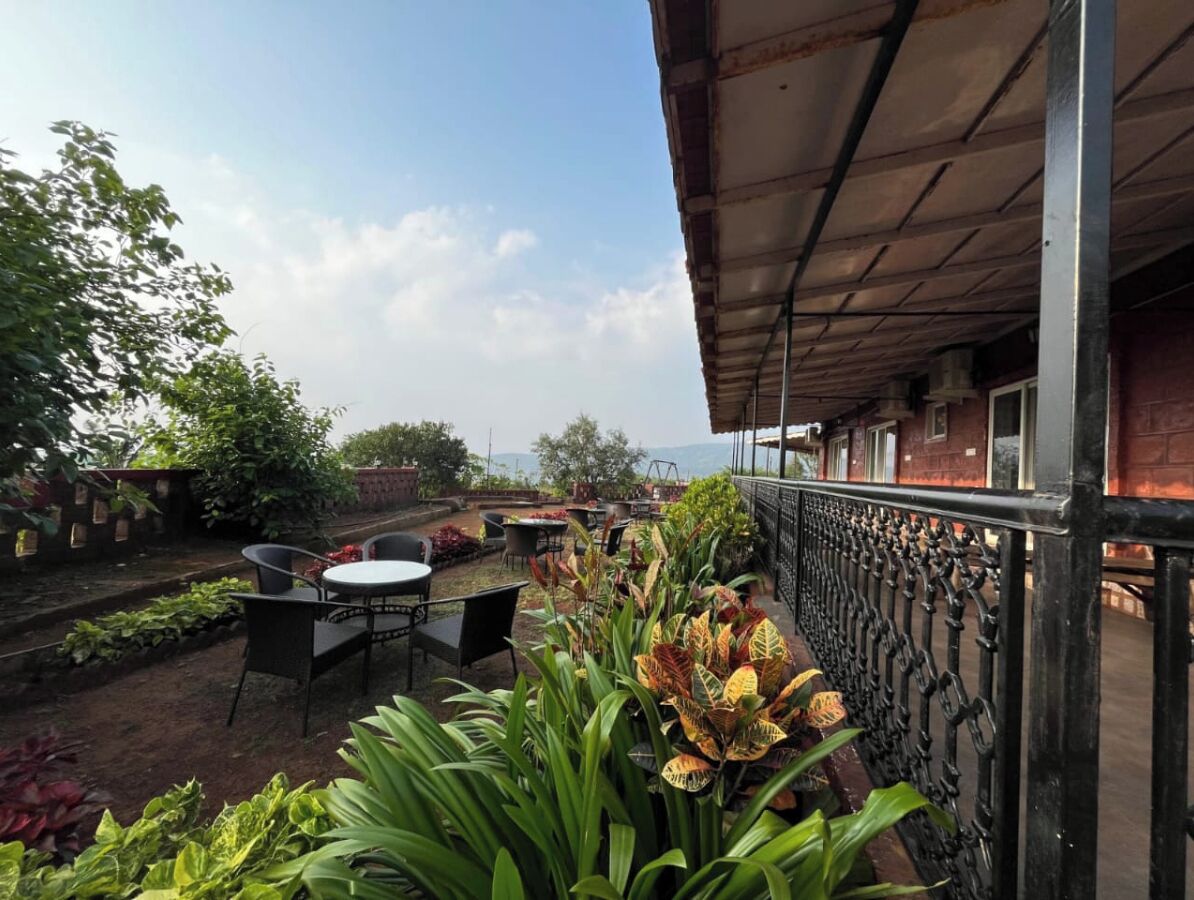 Um terraço no telhado com área de estar externa, rodeado por plantas e um corrimão de metal.