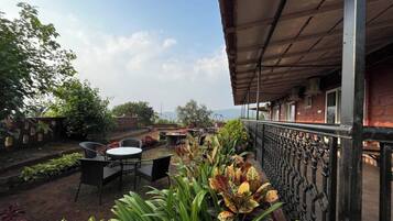 Um terraço no telhado com área de estar externa, rodeado por plantas e um corrimão de metal.