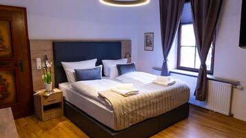 Quarto moderno com uma cama grande, mesas de cabeceira, um criado-mudo, uma luminária de parede e uma janela com cortinas.