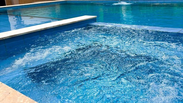 Piscina com água azul cristalina, cercada por um deck revestido e plantas em vasos.