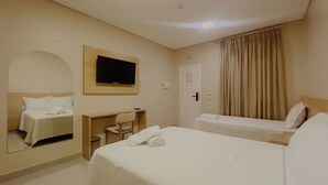 Quarto de hotel com duas camas, uma escrivaninha, uma cadeira, uma televisão e um espelho.