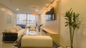 Uma sala de estar moderna com um sofá, poltrona e mesa de centro. Há uma TV montada na parede e um vaso com planta.