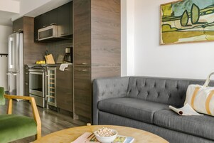 Uma cozinha moderna com micro-ondas, forno e máquina de café, um sofá cinzento e um quadro na parede.