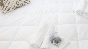 Cama bem arrumada com roupa de cama branca e toalhas enroladas.