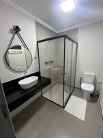 Um banheiro moderno com bancada preta, pia branca, box de vidro e vaso sanitário branco.