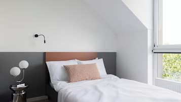 Quarto com cama, mesa de cabeceira, luminária na parede e janela.