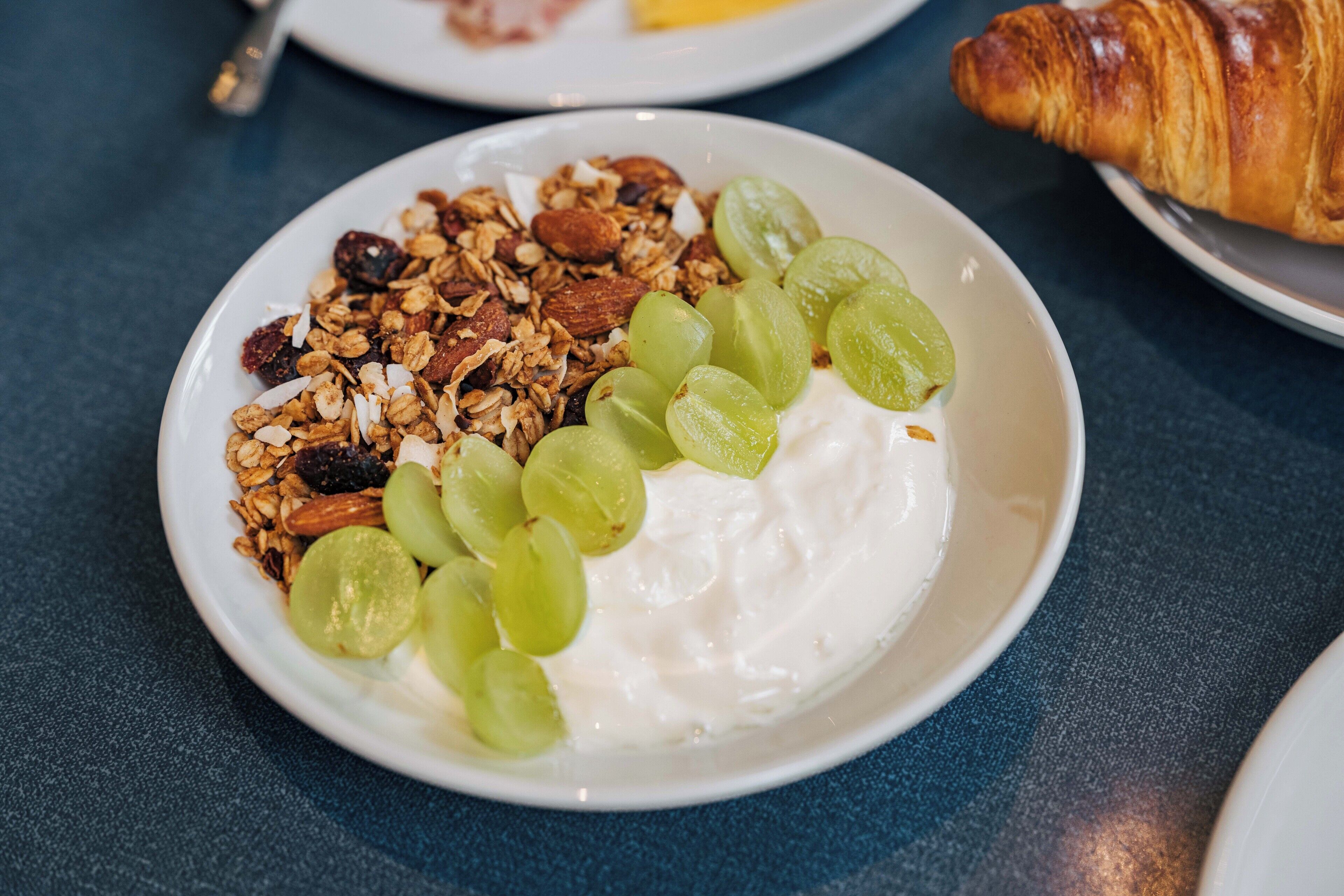 Uma tigela de iogurte com granola e uvas sobre uma mesa.