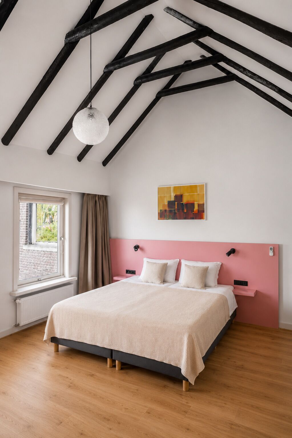 Quarto com cama, janela, teto com vigas aparentes e luminária fixada na parede.