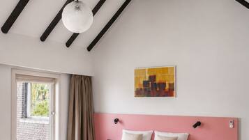 Quarto com cama, janela, teto com vigas aparentes e luminária fixada na parede.