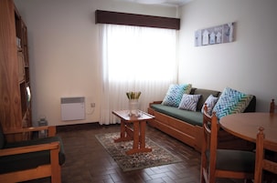 Uma sala de estar com sofá, móveis de madeira, uma mesinha com um vaso e uma obra de arte na parede.