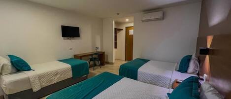 Quarto de hotel com duas camas de solteiro, uma escrivaninha, uma cadeira, uma televisão e um aparelho de ar condicionado.
