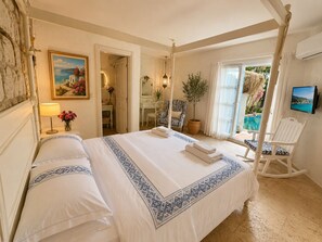 Quarto de hotel com uma cama grande, televisão, cadeira e vista para uma piscina.
