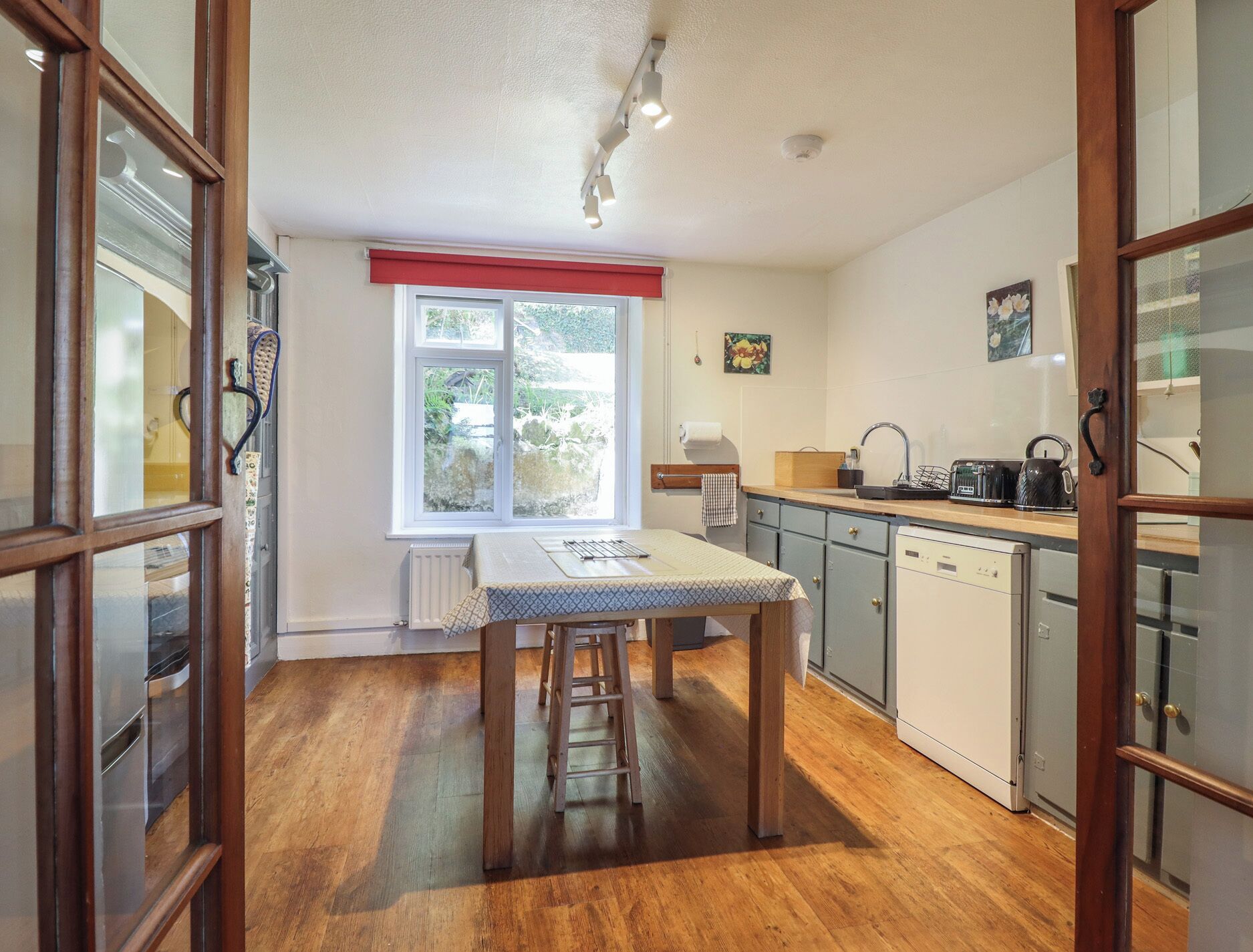 Uma cozinha com piso de madeira, uma mesa com toalha, uma janela com vista e uma máquina de lavar louça.