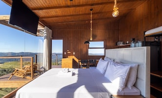 Quarto com uma cama grande, teto de madeira, televisão e vista para o exterior.