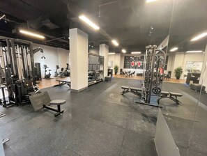Uma academia com diversos equipamentos de ginástica, um banco e um espelho grande na parede.