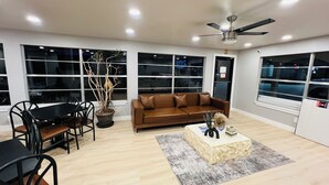 Uma sala de estar moderna com um sofá de couro marrom, uma mesa de jantar com cadeiras, um vaso de plantas e um ventilador de teto.