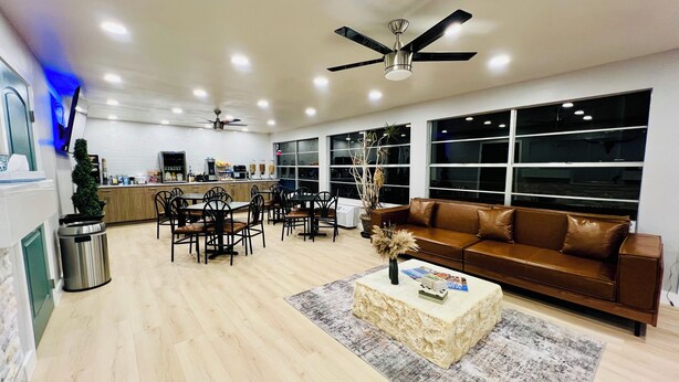 Uma sala de estar moderna com um sofá de couro marrom, uma mesa de centro com objetos decorativos e uma área de jantar com cadeiras, além de uma cozinha ao fundo.