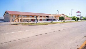 Um motel com estrutura em dois andares, área de estacionamento coberta e placa visível do motel.