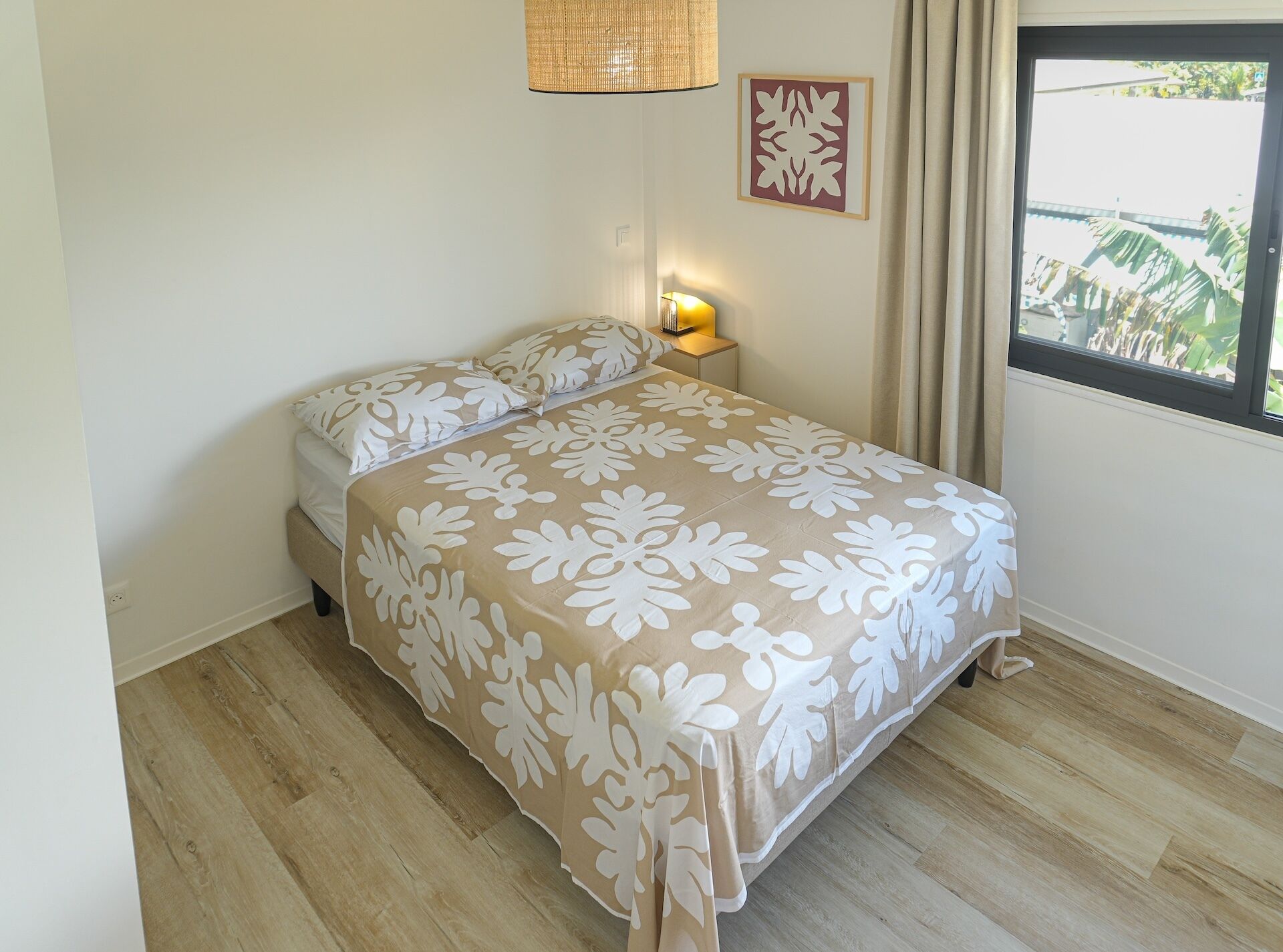 Quarto com cama, luminária de cabeceira, obra de arte na parede e janela com cortinas.