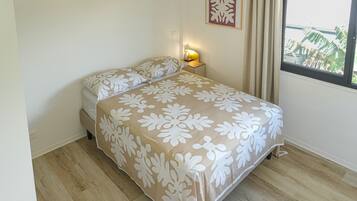 Quarto com cama, luminária de cabeceira, obra de arte na parede e janela com cortinas.