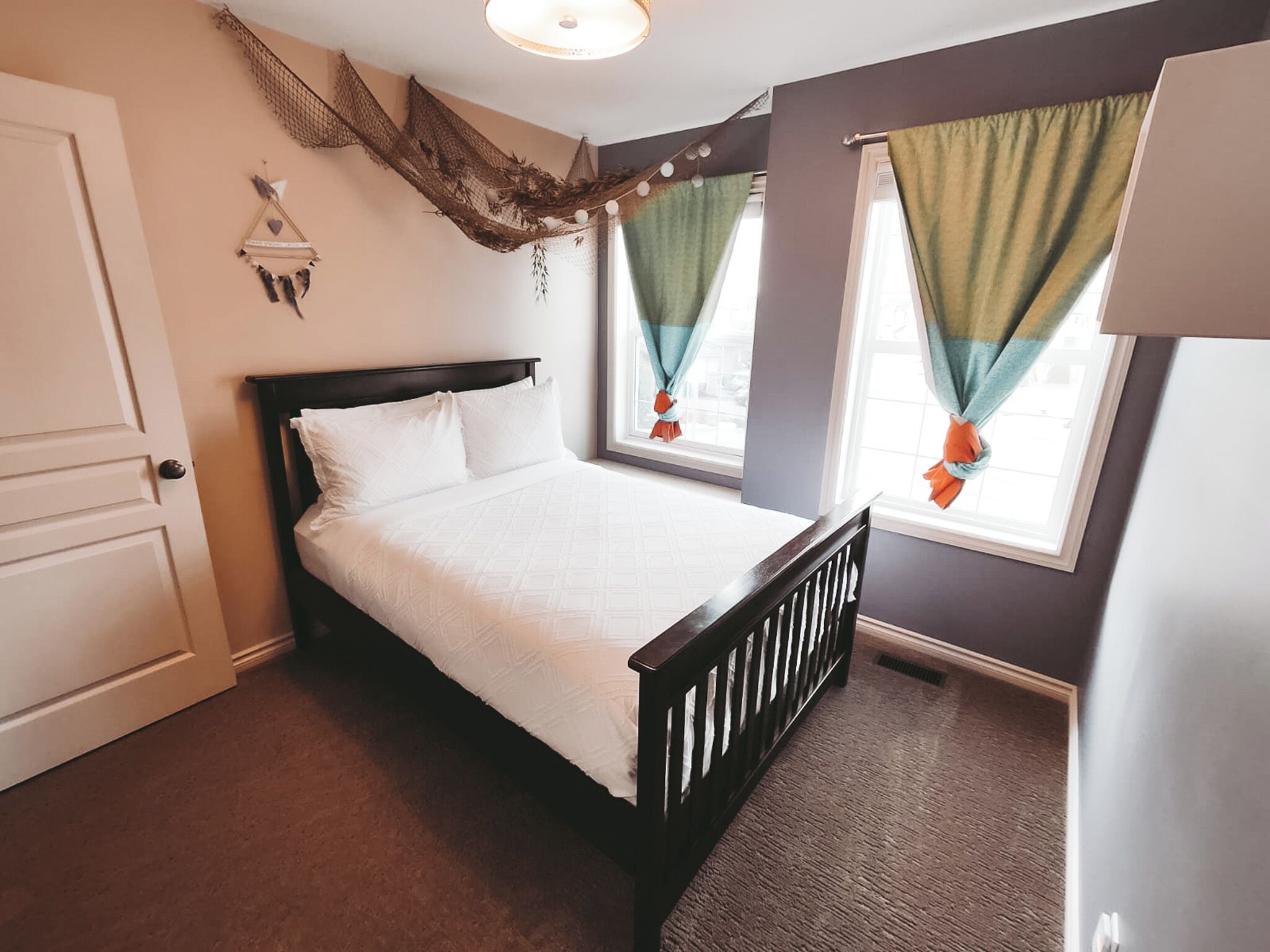 Quarto com cama, porta e duas janelas com cortinas.