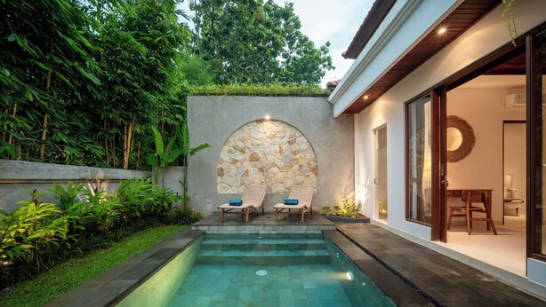 Piscina com duas espreguiçadeiras e uma parede de pedra com um desenho circular.