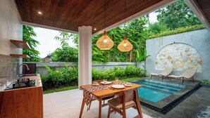 Uma área moderna para refeições ao ar livre, com piscina, móveis de madeira e luminárias penduradas.