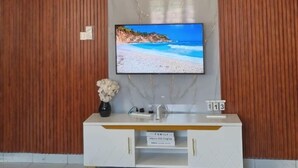 Uma sala de estar moderna com uma TV de tela plana fixada na parede, lambris de madeira, um rack branco e um ventilador de teto.