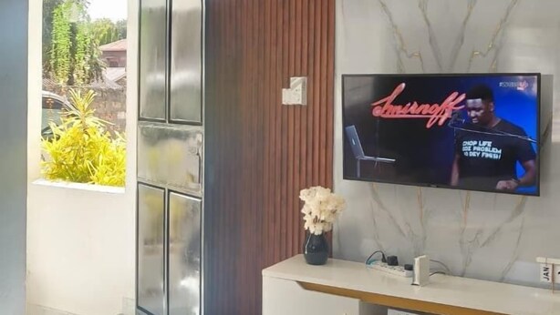 Uma sala de estar moderna com uma TV fixada em uma parede de mármore, um armário branco com puxadores dourados e uma mesa de vidro.