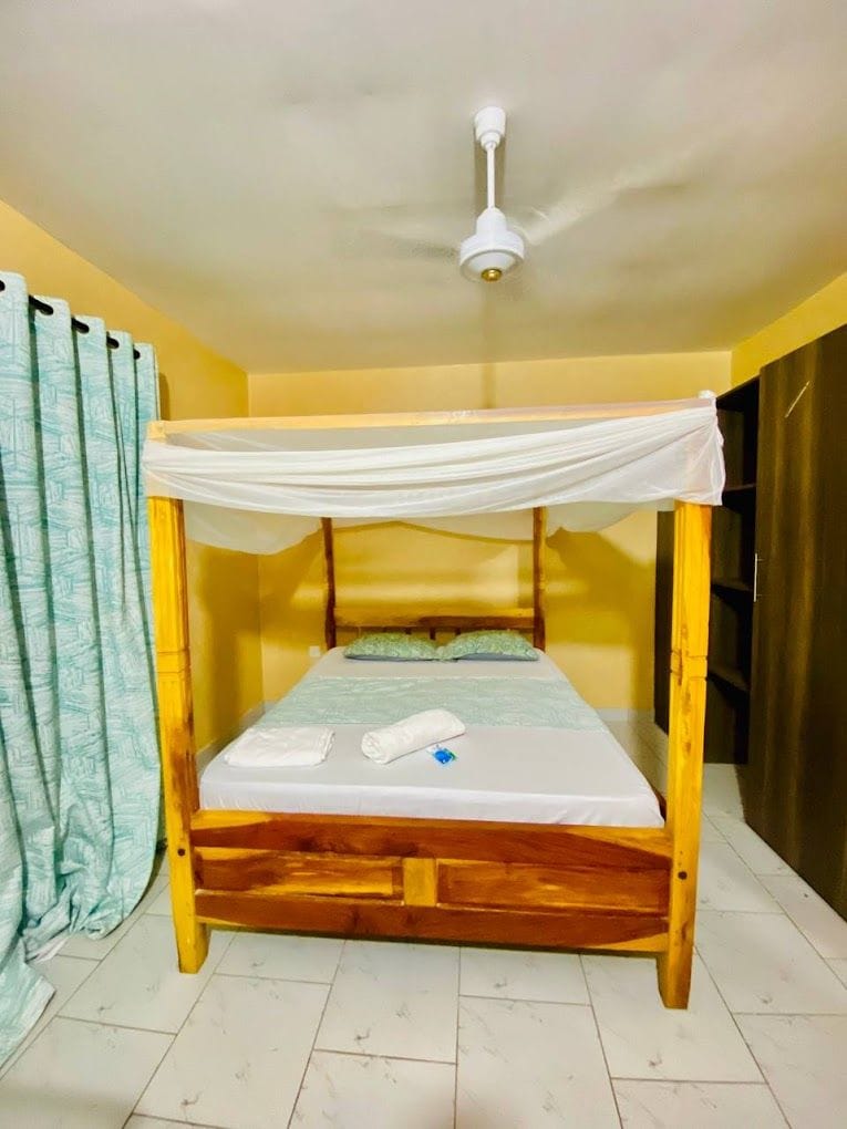 Uma cama de solteiro com dossel, um ventilador de teto e uma cortina.