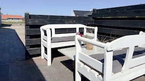 Uma área de estar ao ar livre com mesa e bancos, cercada por uma vedação de madeira.