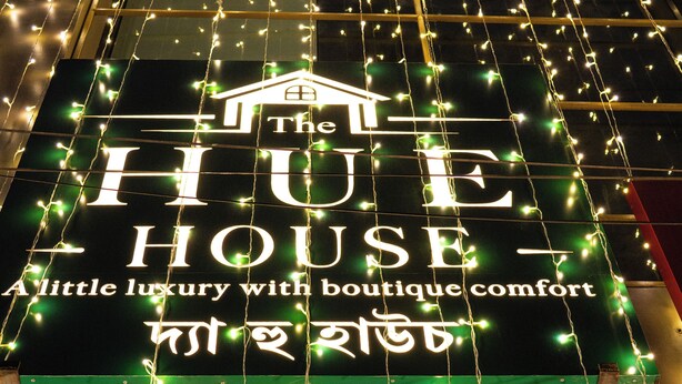 Um letreiro com o texto 'The HUE HOUSE - A little luxury with boutique comfort' e um detalhe decorativo abaixo.