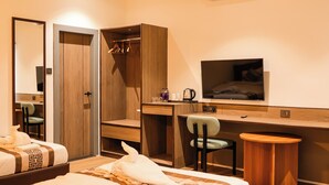 Quarto de hotel com duas camas, uma escrivaninha, uma cadeira, uma televisão e um guarda-roupa.