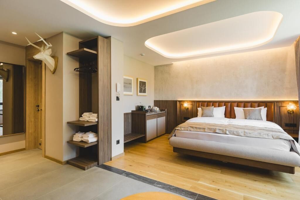 Quarto moderno com cama, estantes de madeira, um cabideiro e luminária fixada na parede.